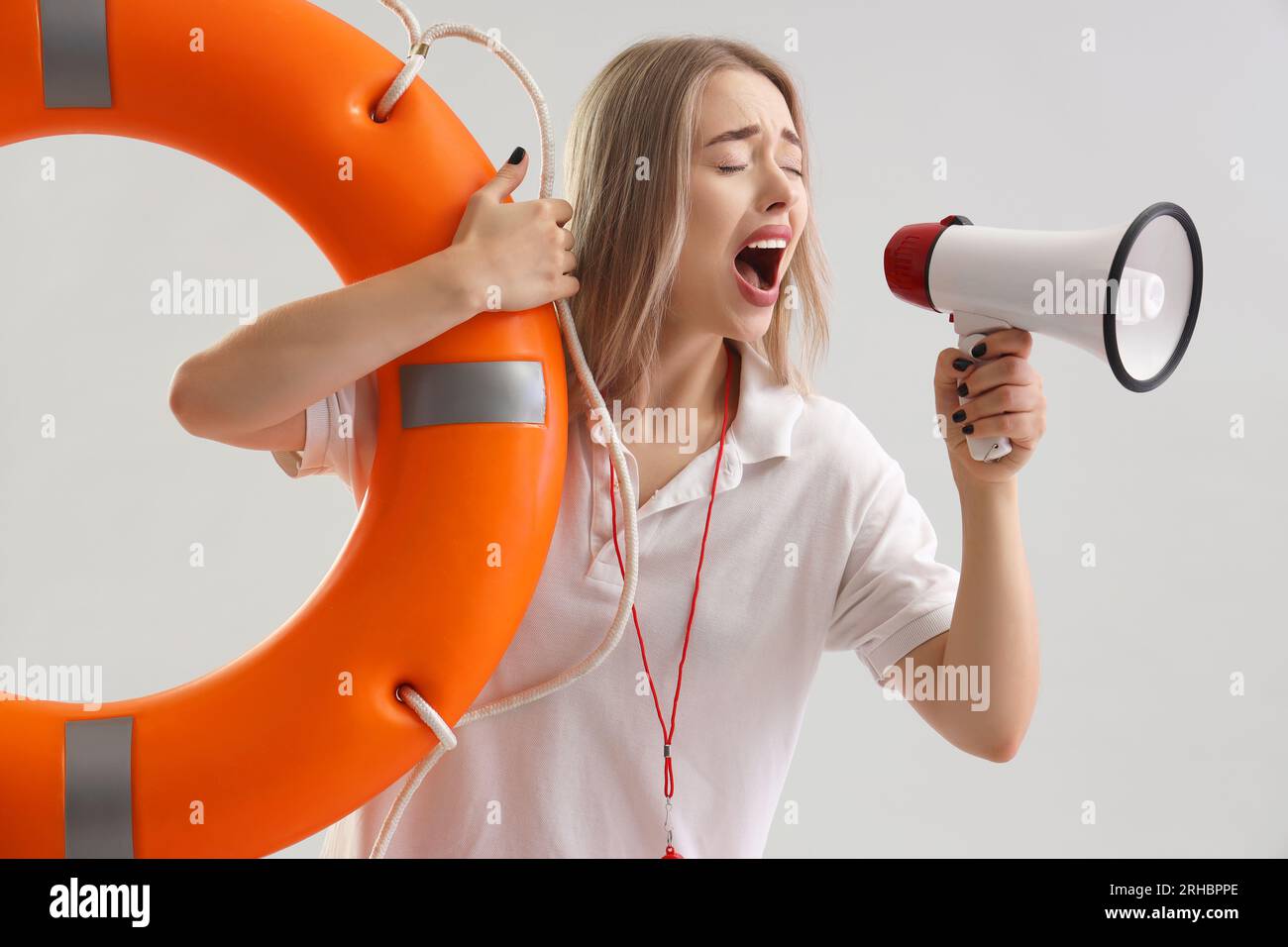 Female lifeguard with ring buoy shouting into megaphone on light ...