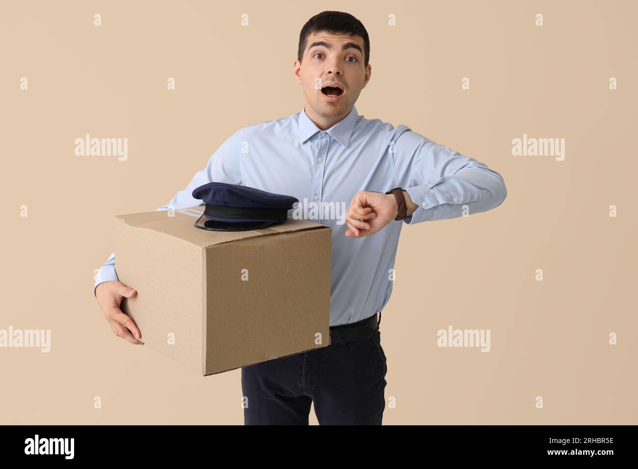 Shocked young postman with wristwatch and parcel on beige background ...