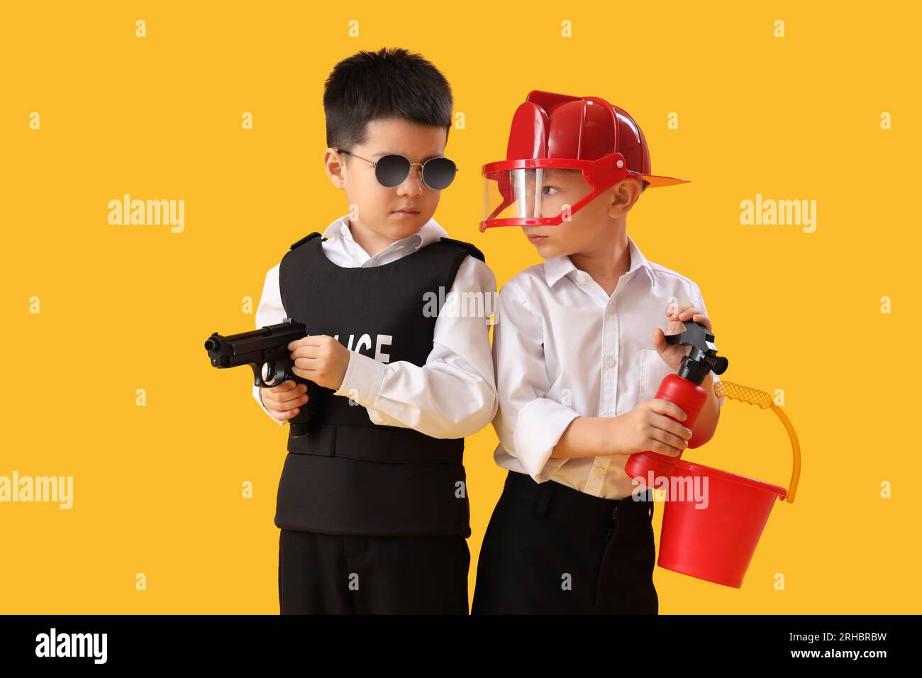Cute little policeman and firefighter on yellow background Stock Photo ...