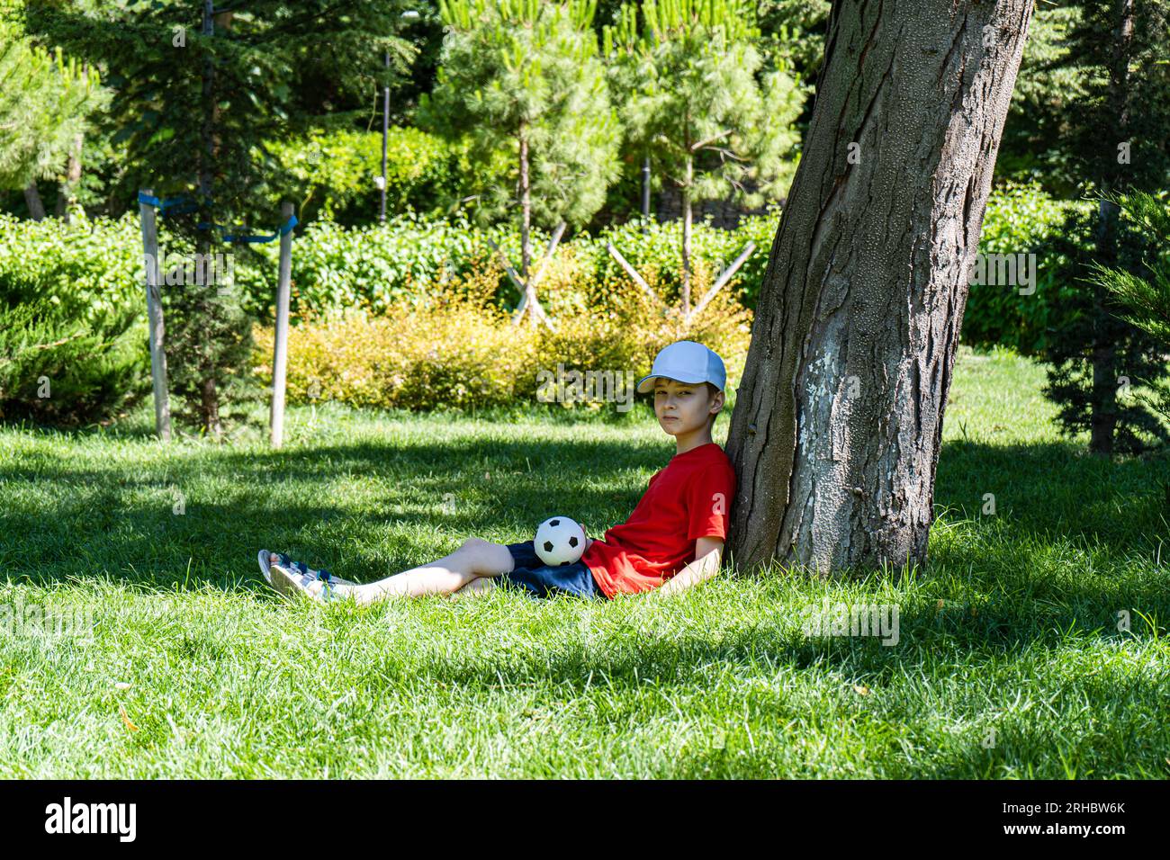 Boy sitting under a tree in summer with a football, Georgia Stock Photo ...