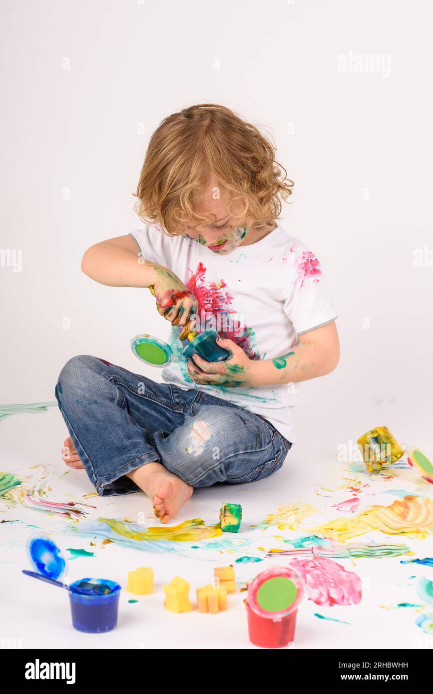 Full body of curious dirty boy with can of paint sitting on messy floor ...