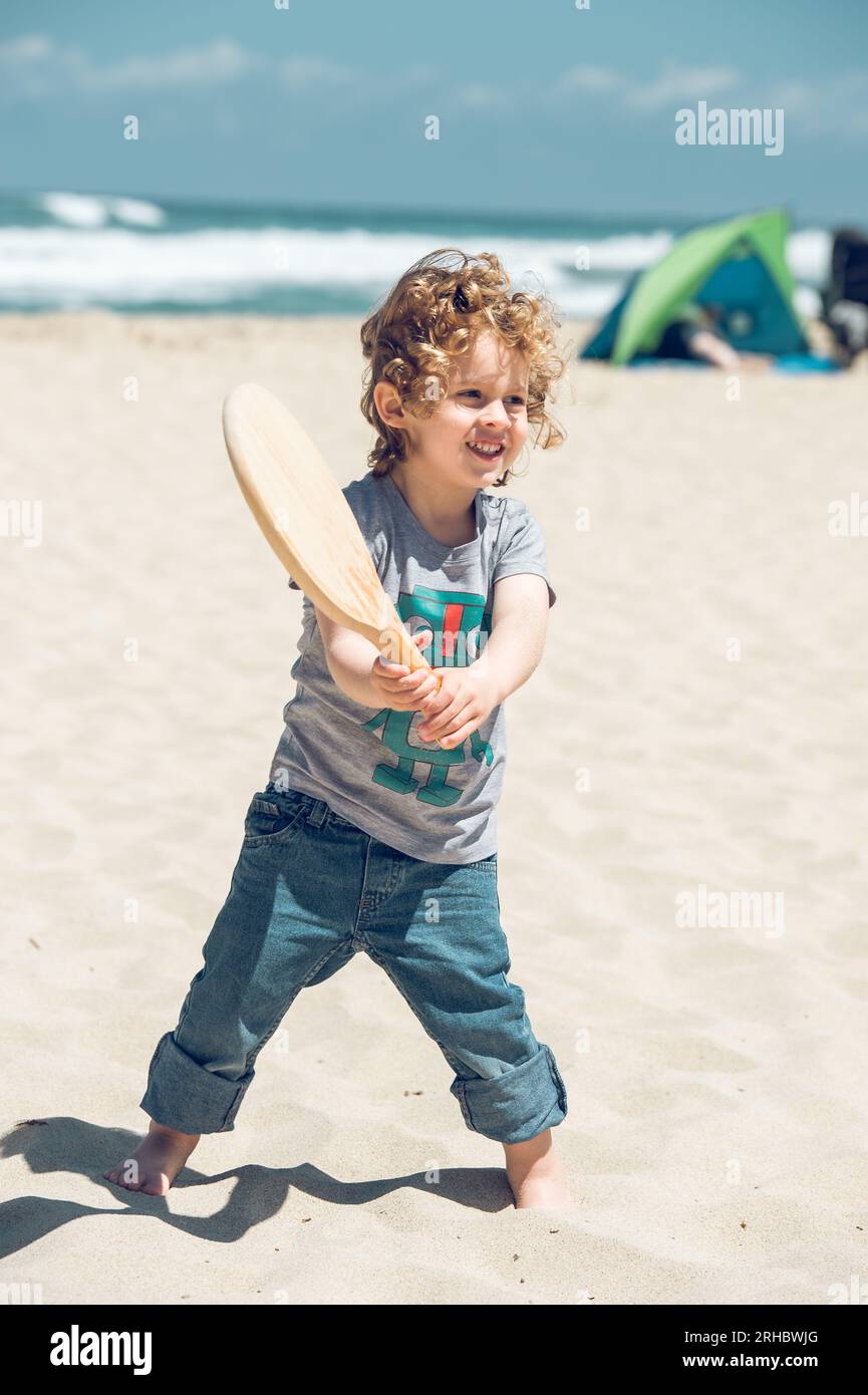 Full body of positive barefoot boy playing with wooden tennis racket on ...