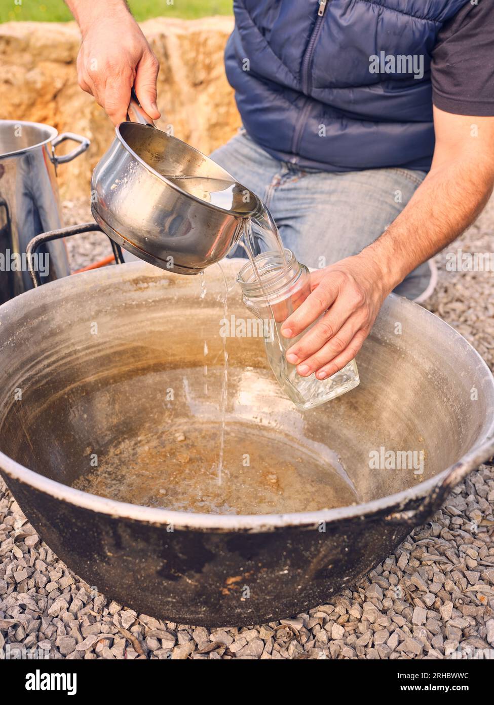 From above of crop unrecognizable man pouring water from stewpot into glass jar over metal basin ...
