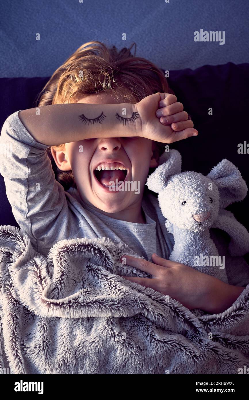 From above of annoyed boy lying in bed with plush toy and screaming ...