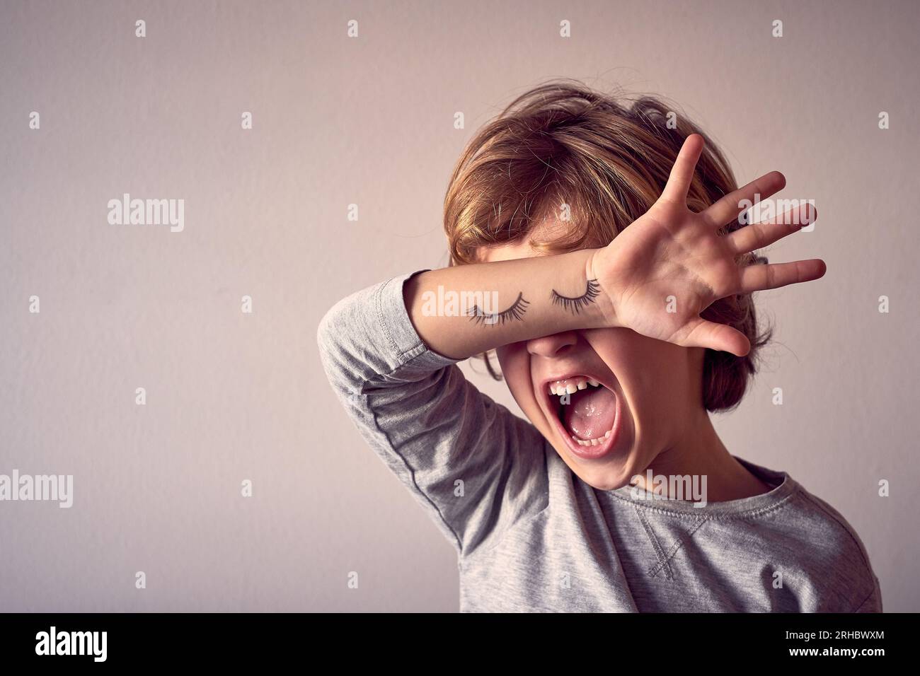 Irritated boy screaming loud with mouth opened and covering eyes with ...