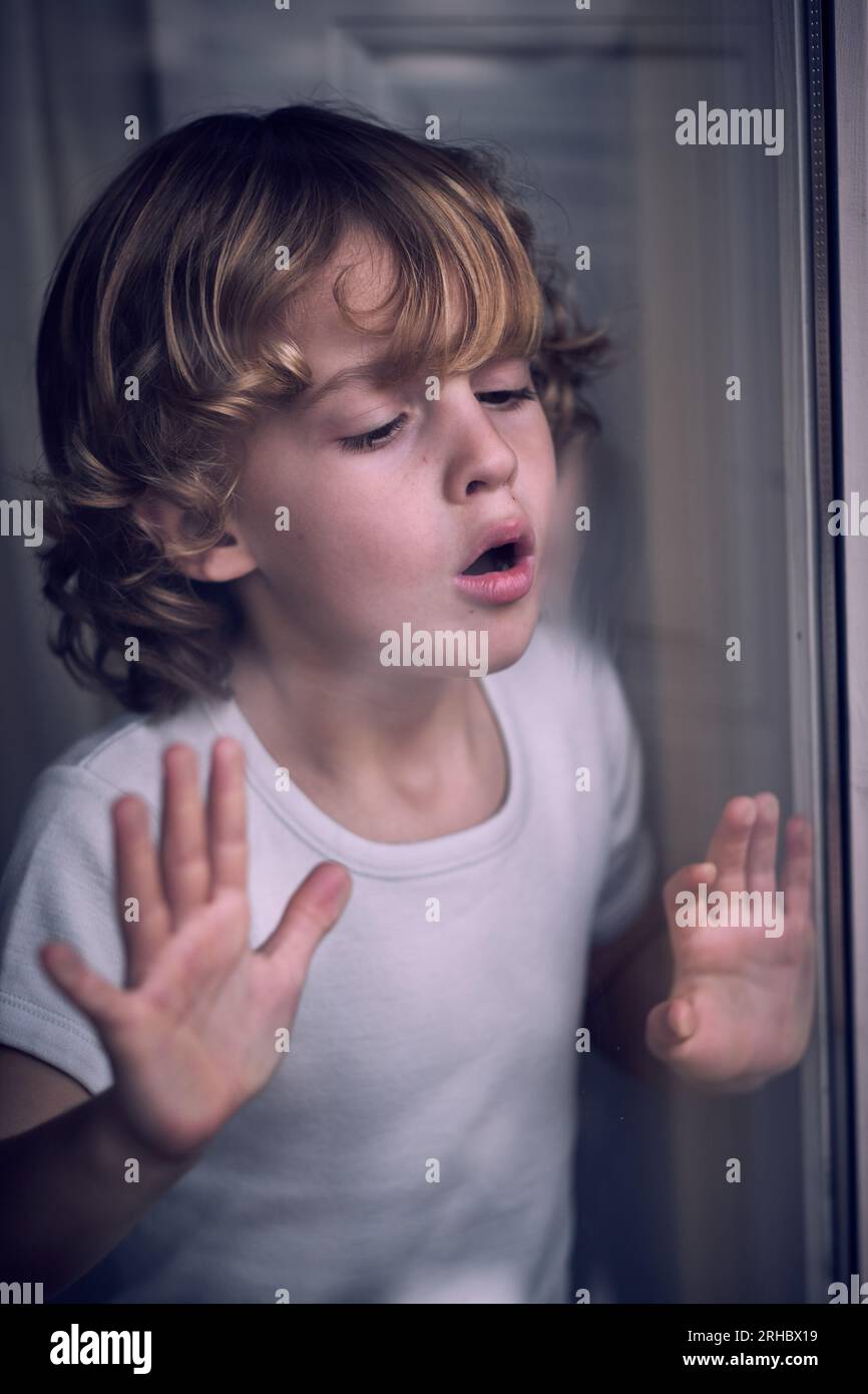 Through glass of cute little bot with curly blond hair in t shirt ...