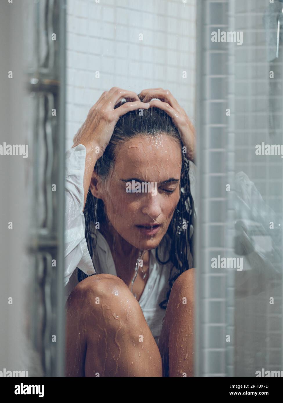 Sad female with wet dark hair in white shirt and with closed eyes ...