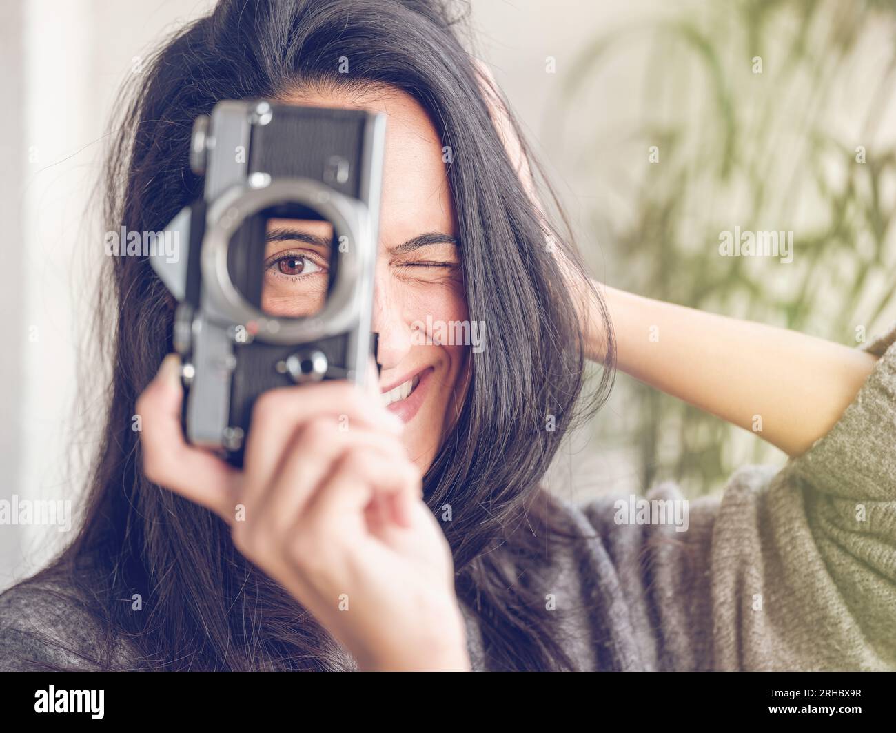 Smiling female with dark hair looking through vintage film photo camera ...