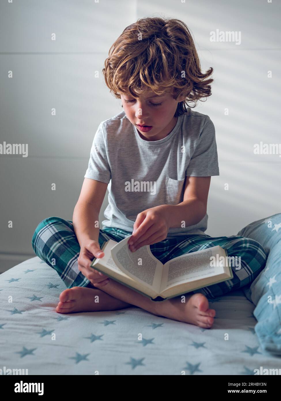 Full body of adorable curly haired little boy in pajamas sitting with ...