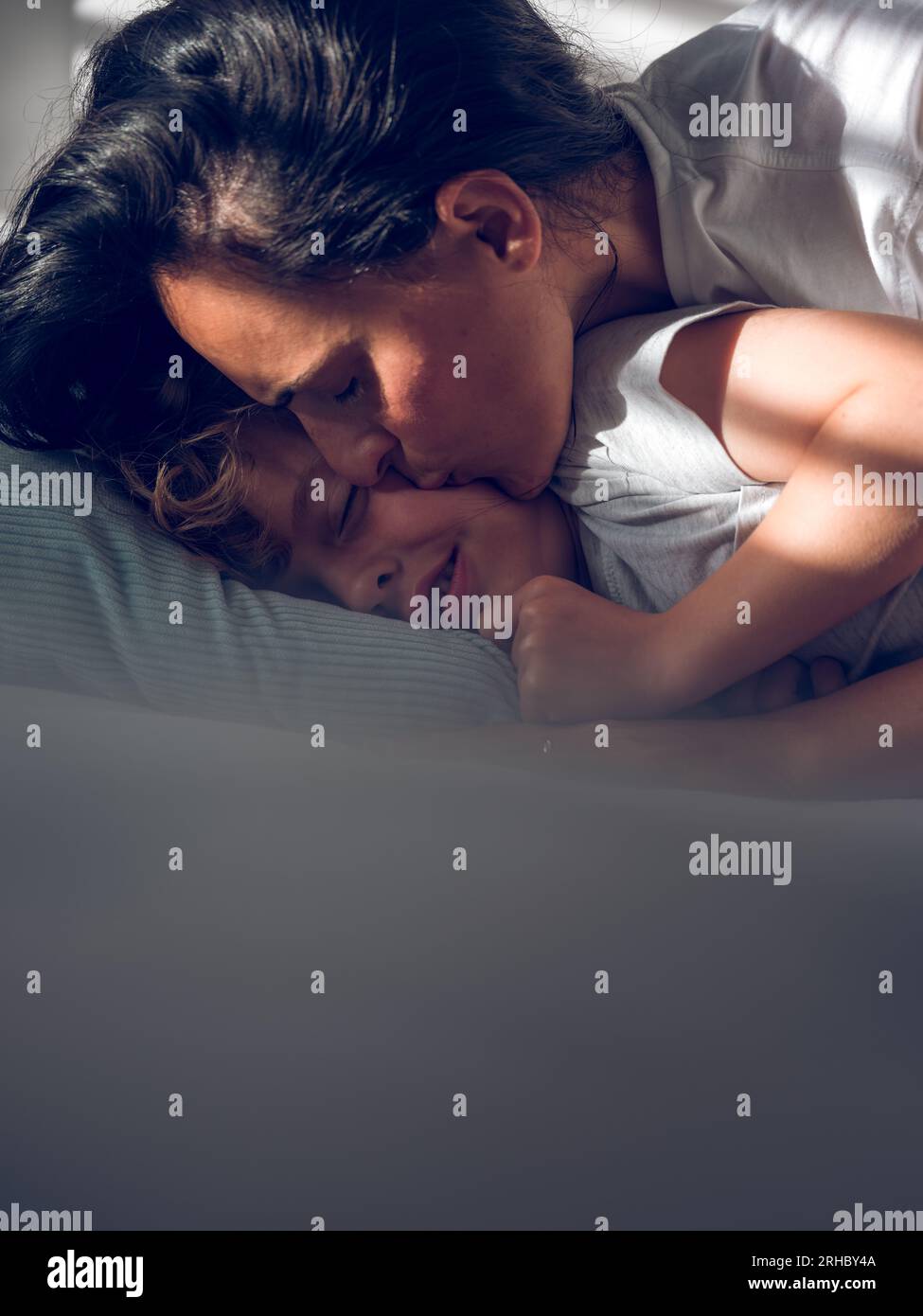 Tender mother kissing cheek of cute son sleeping on comfortable white ...