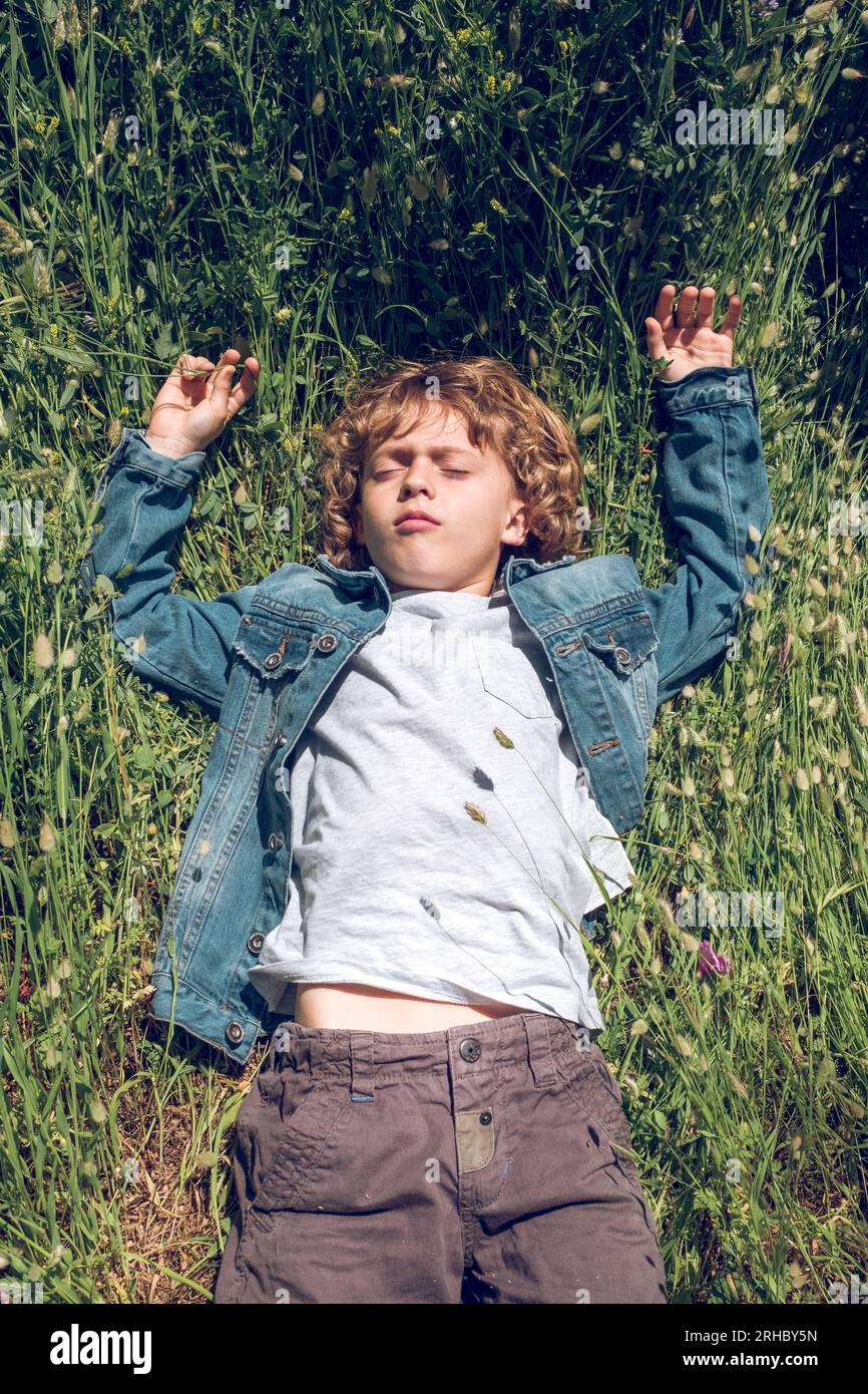 From above of preteen curly haired adorable boy napping on green grass ...