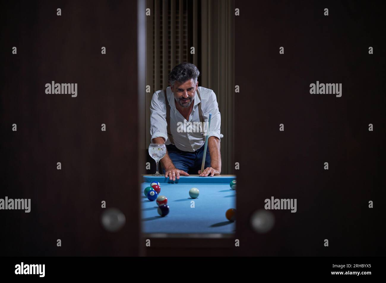 Through doors shot of positive adult man leaning on blue pool table ...
