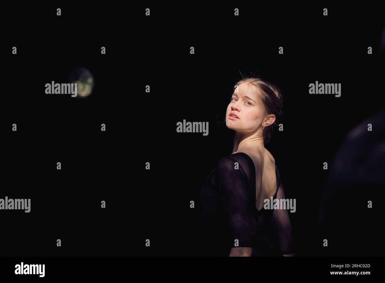 Back view of tender female ballet dancer standing against darkness in ...