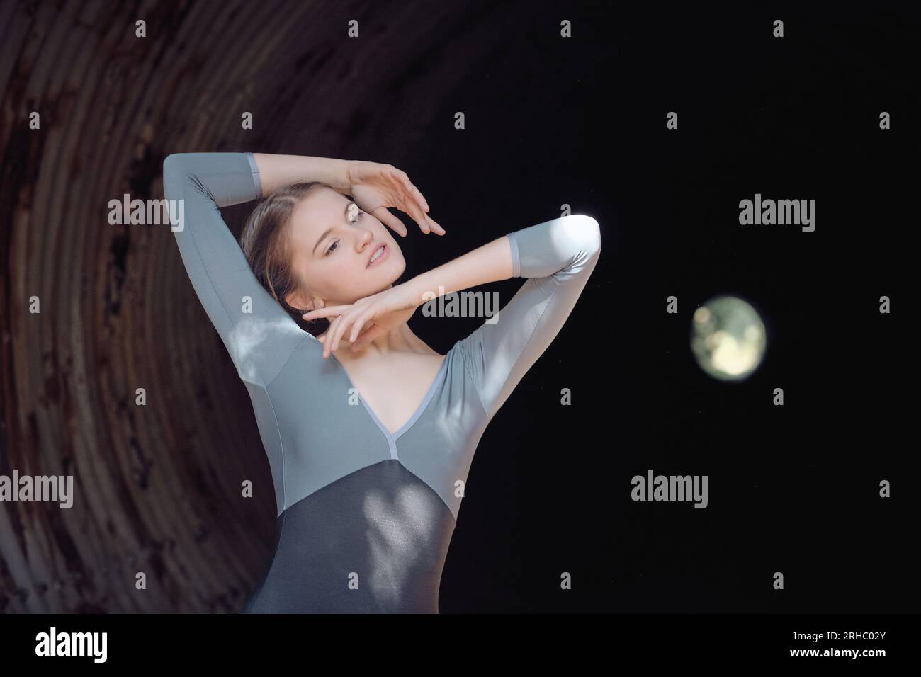 Charming young slim ballet dancer with arms at head looking into ...