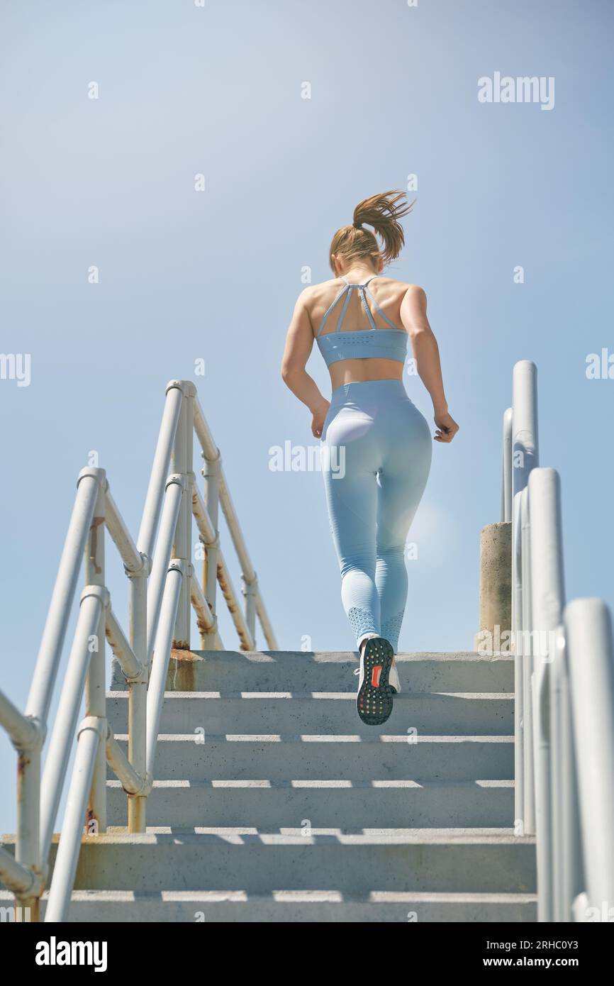 Low angle back view of unrecognizable female runner jogging on ...