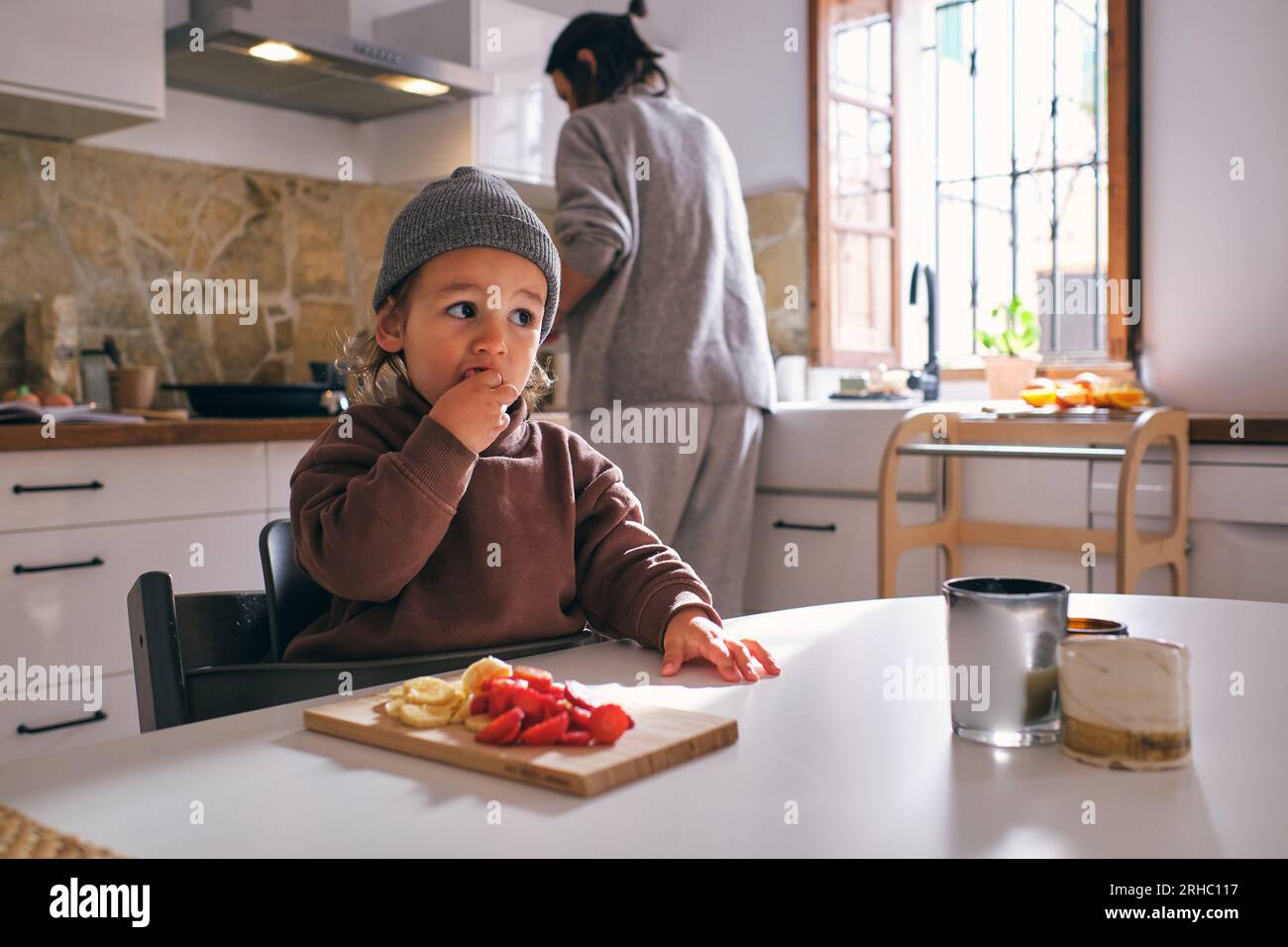 Adorable little child sitting on chair at table and eating delicious ...