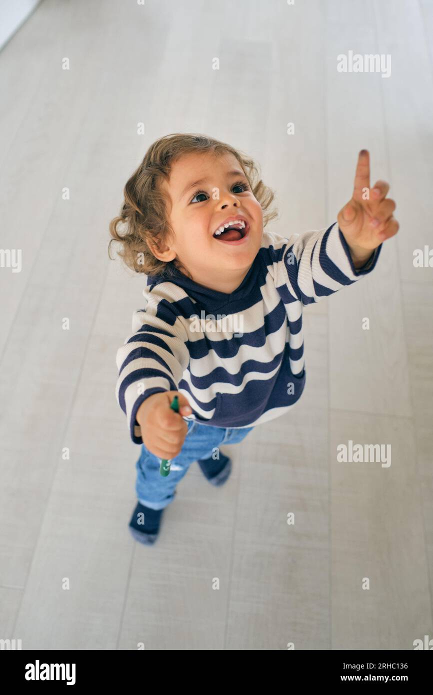 High angle full body of adorable excited toddler with curly hair in ...