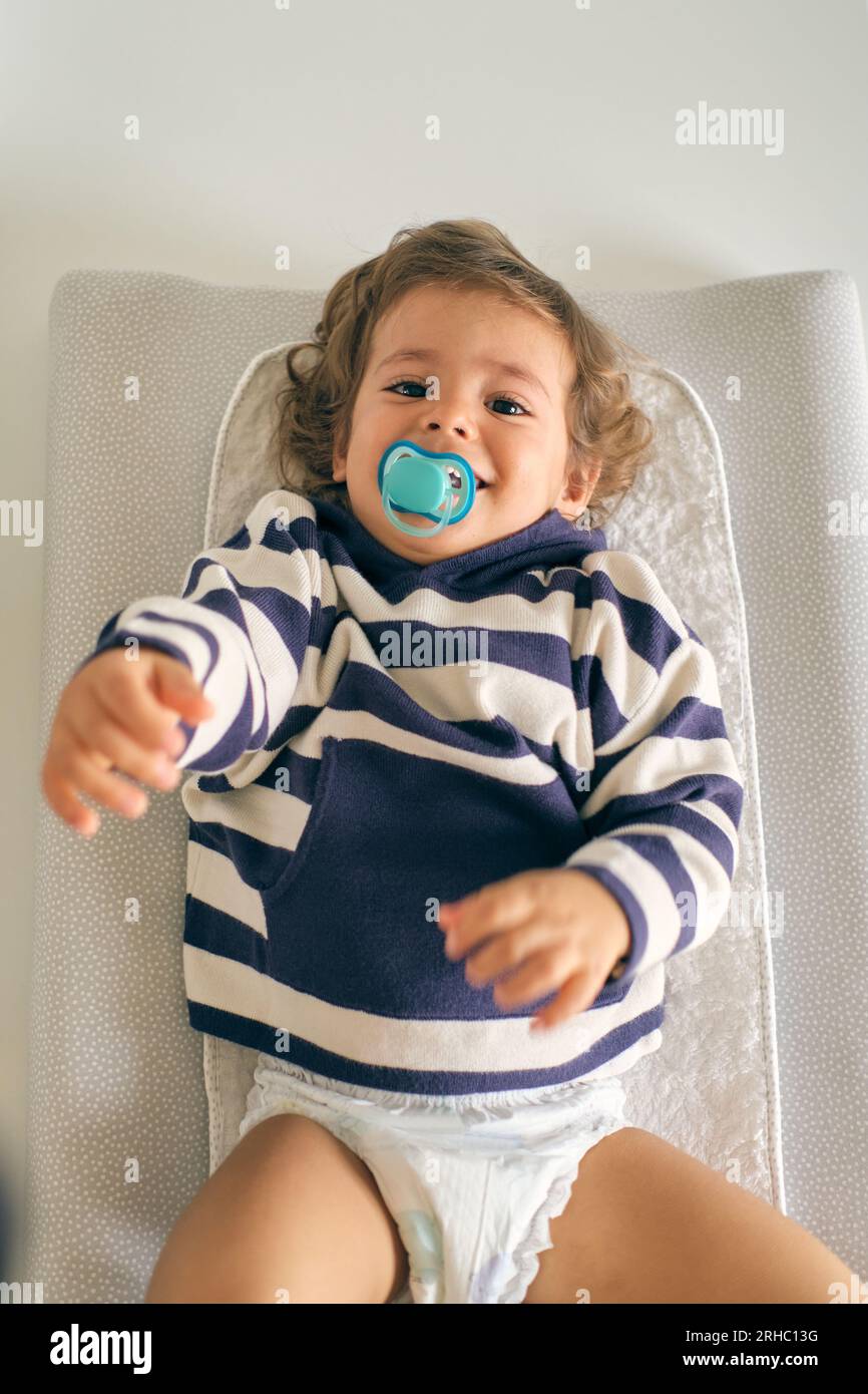 Carefree little boy with blue pacifier in nappy smiling and looking at ...