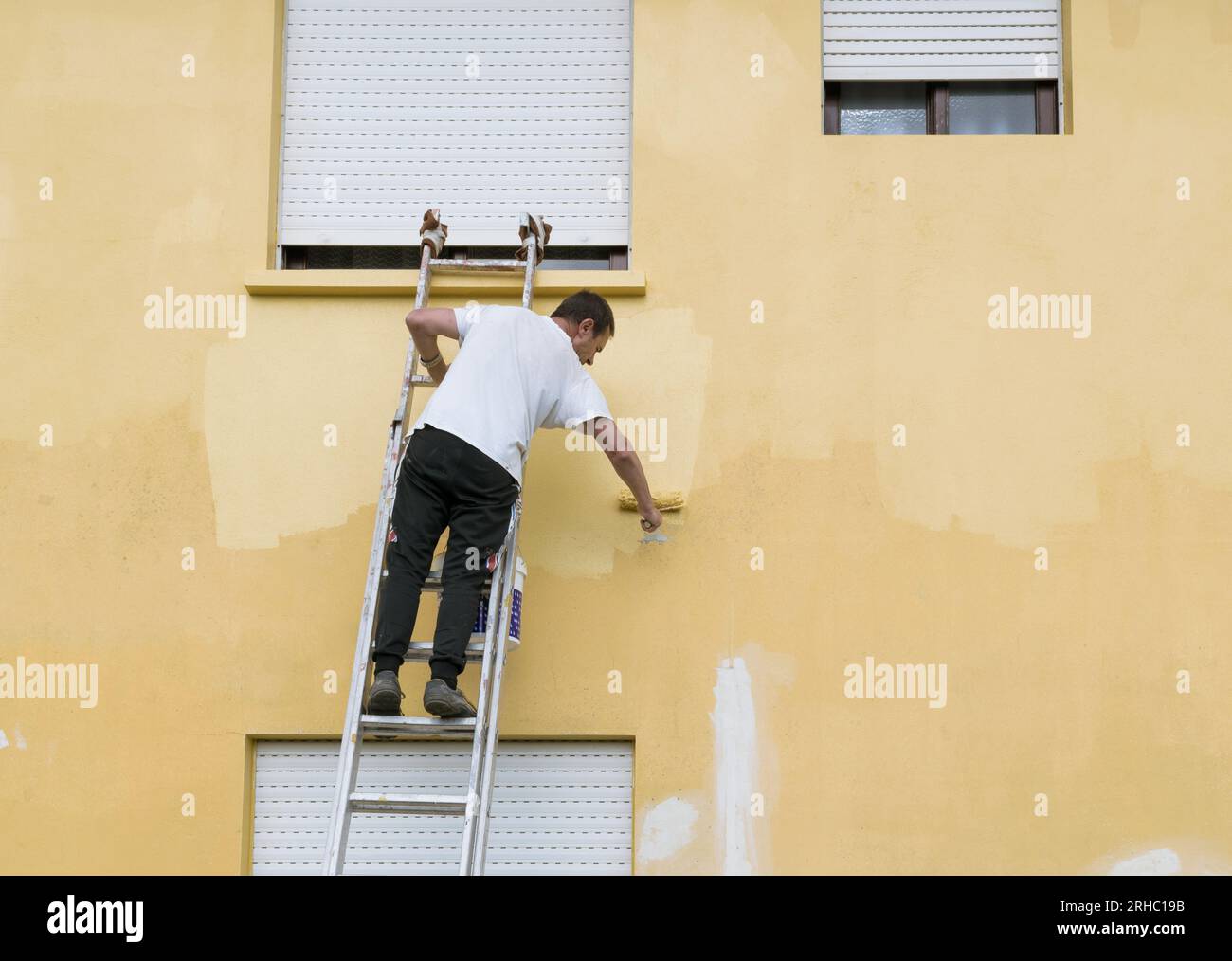 Rear view of a man on a ladder painting a house yellow, Spain Stock ...