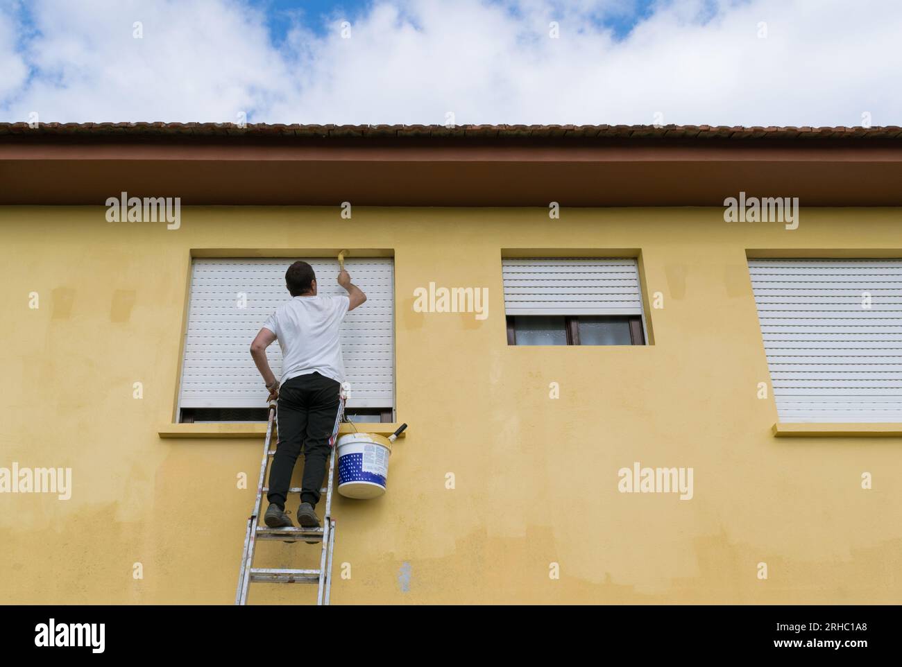 Rear view of a man on a ladder painting a house yellow, Spain Stock ...