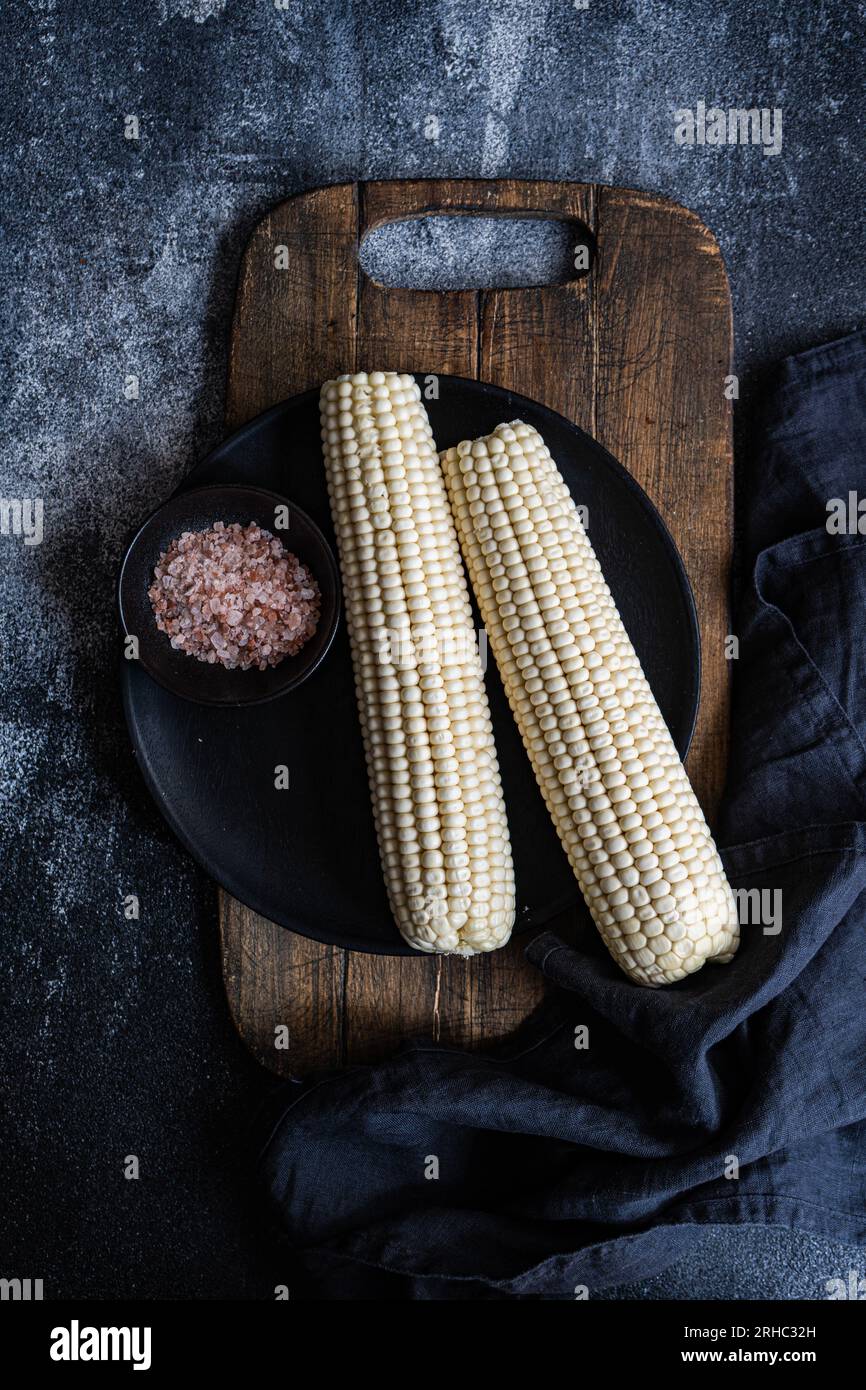 Overhead view of two corn cobs with pink Himalayan salt on a chopping ...