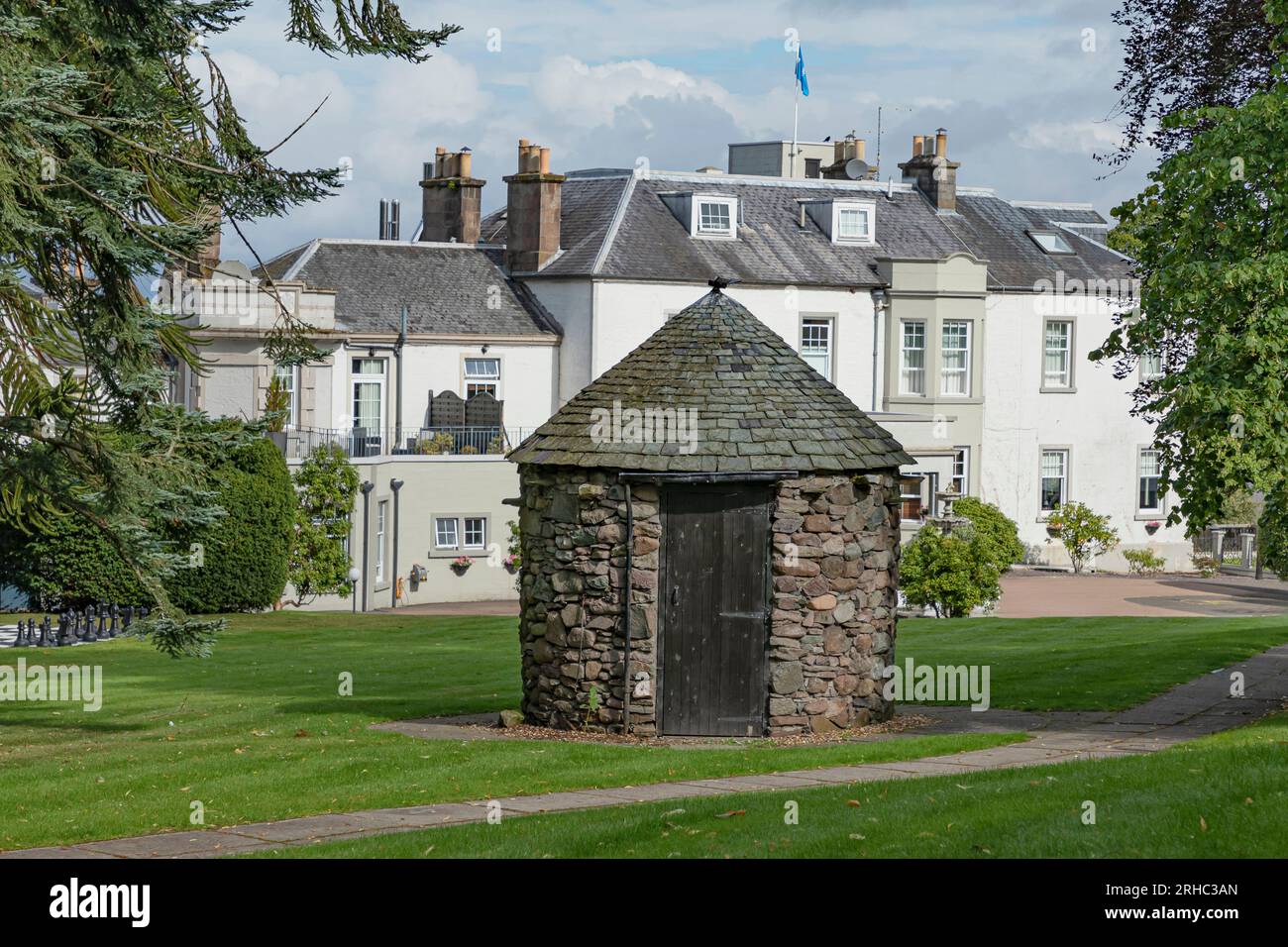 Stone dovecot infront of a white building in Scotland with a flag ...