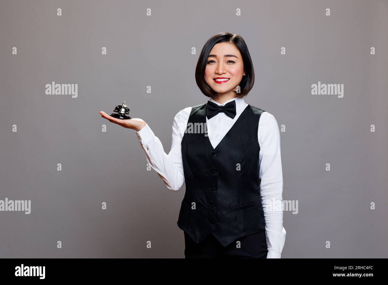 Restaurant receptionist in uniform holding bell in hand, smiling and ...
