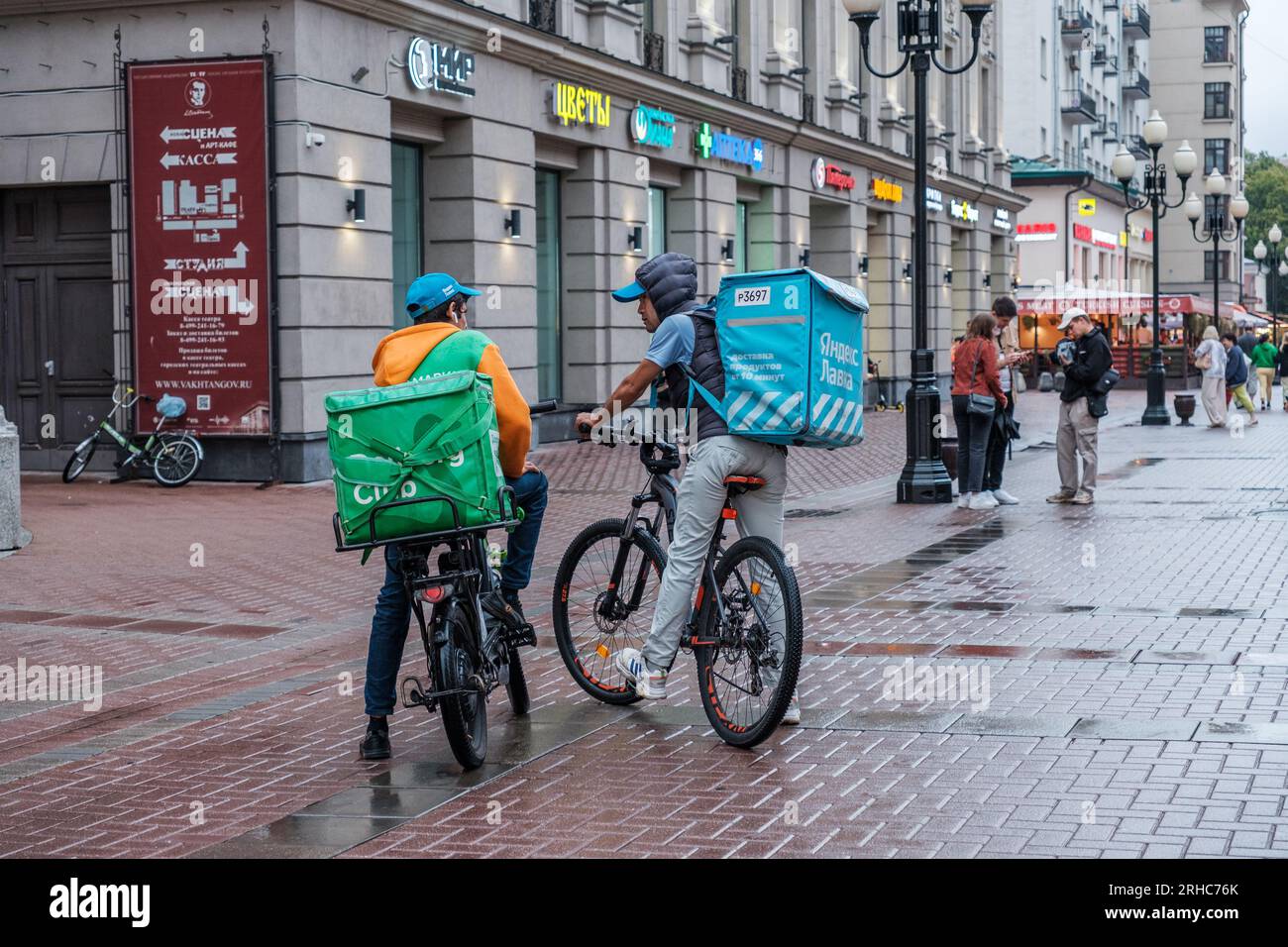 Two Yandex Food couriers on bicycles with large thermal bags on Stary ...