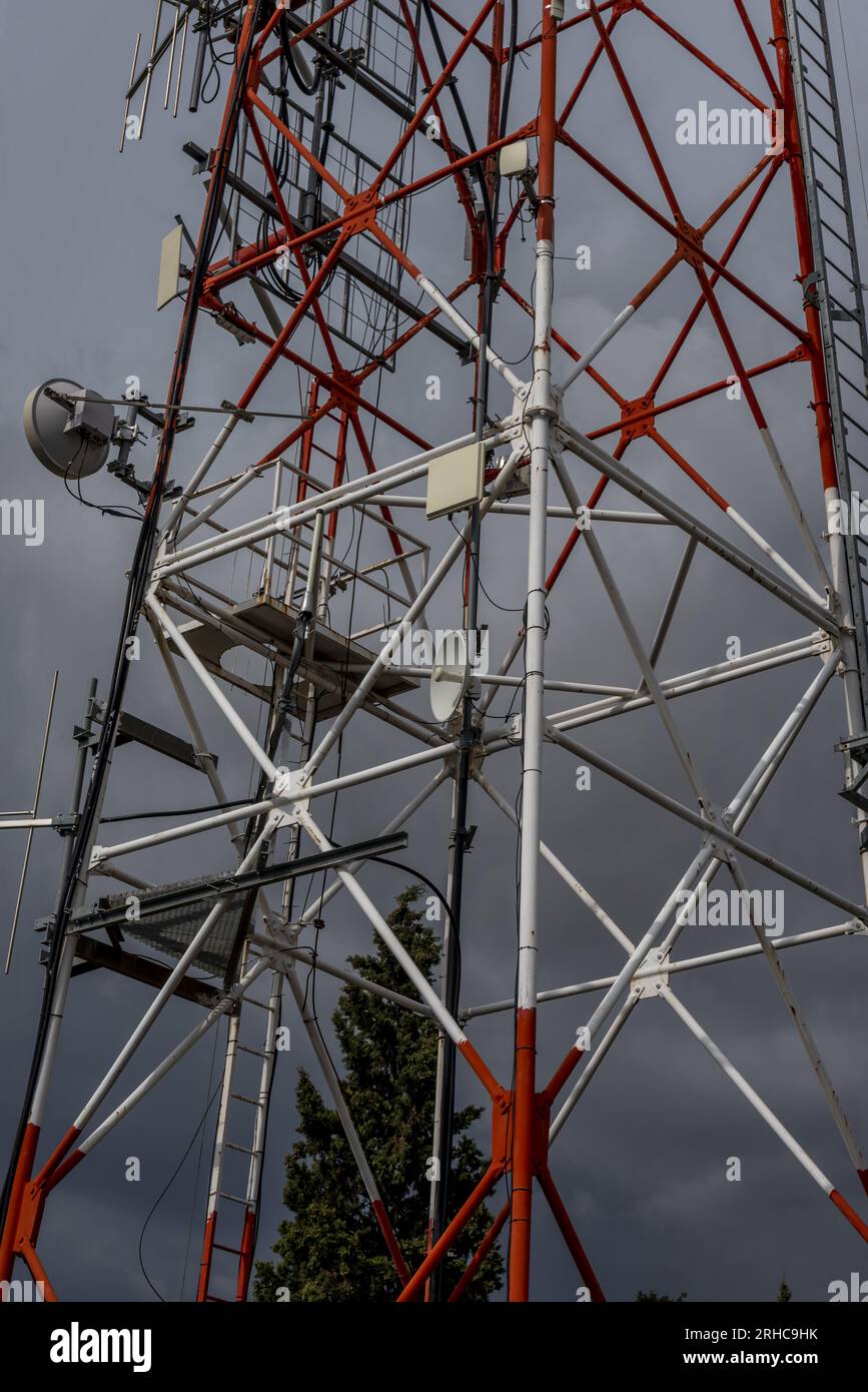 Metal telecommunications tower painted white and red with stairs and access platforms to several ...