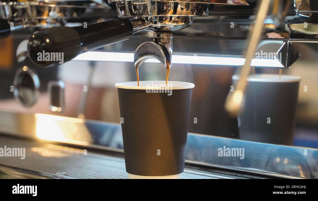 Fresh espresso. Close-up of flowing coffee from machine into paper cup ...
