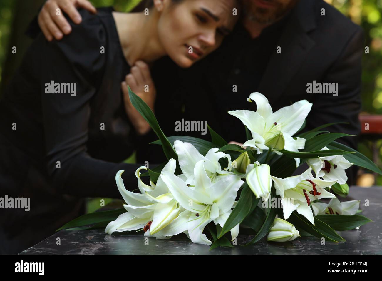 Sad couple mourning near granite tombstone with white lilies at ...