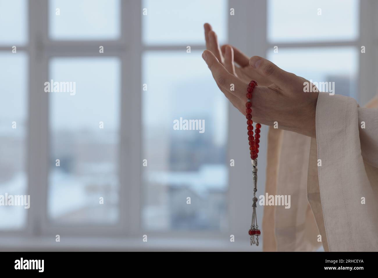 Muslim man with misbaha praying near window indoors, closeup. Space for ...