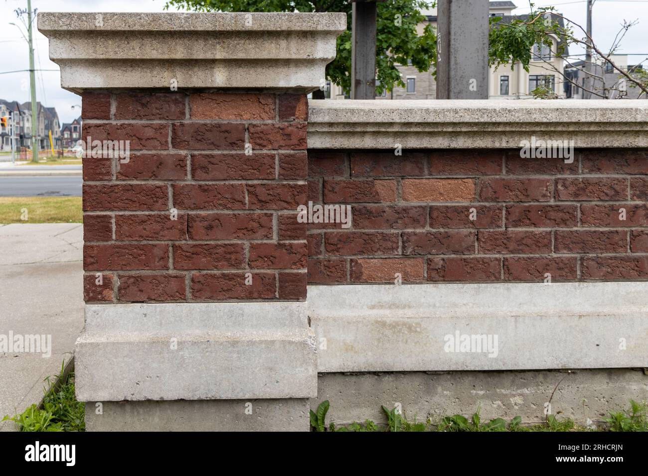 Red brick wall with white mortar and light grey stone pillar on grassy ...