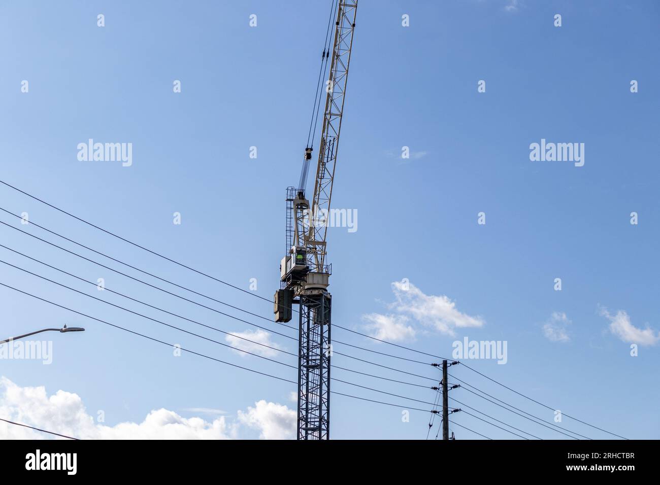 Yellow and black construction crane lifting load near power lines - blue sky with clouds Stock ...