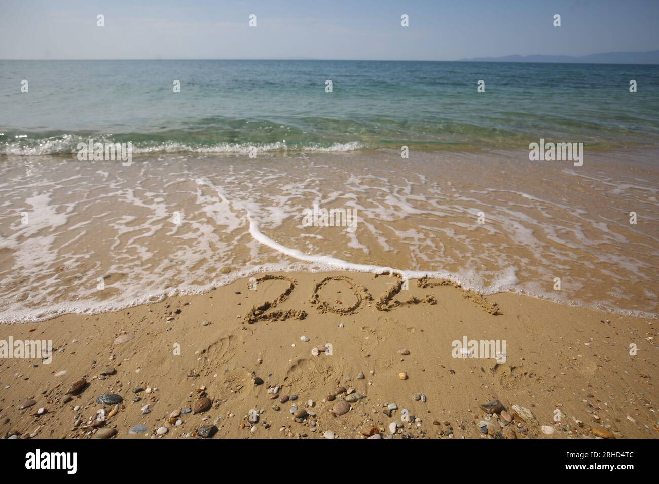 New Year 2024, lettering on the beach with wave and clear blue sea. Numbers 2024 year on the sea ...