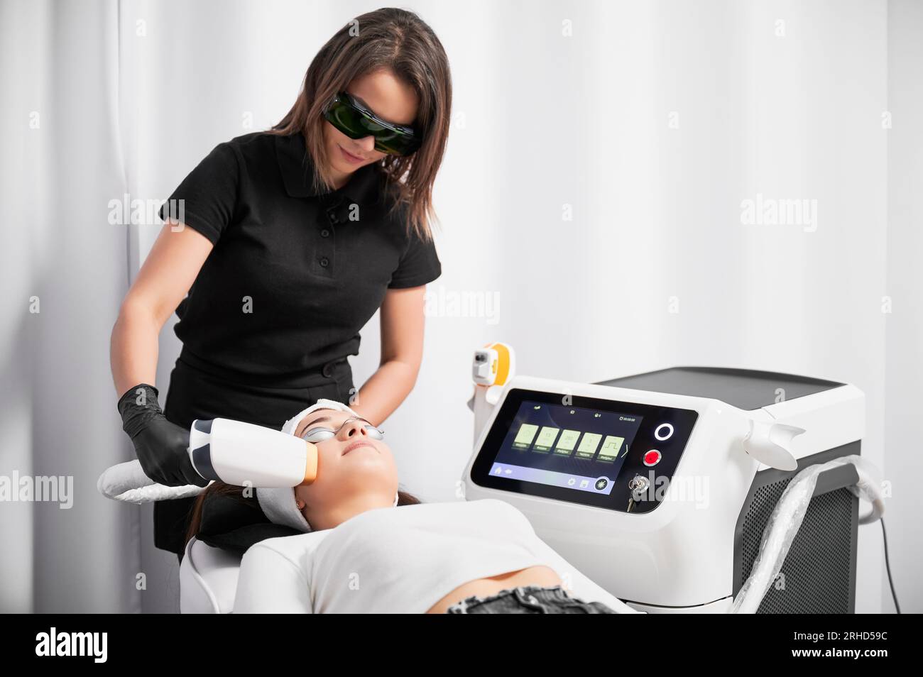 Cosmetologist in safety glasses using diode laser device while ...