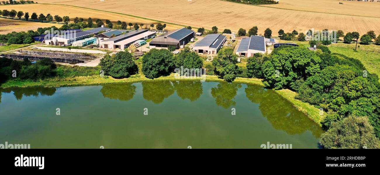Modern farm with buildings that have solar panels behind a pond in ...