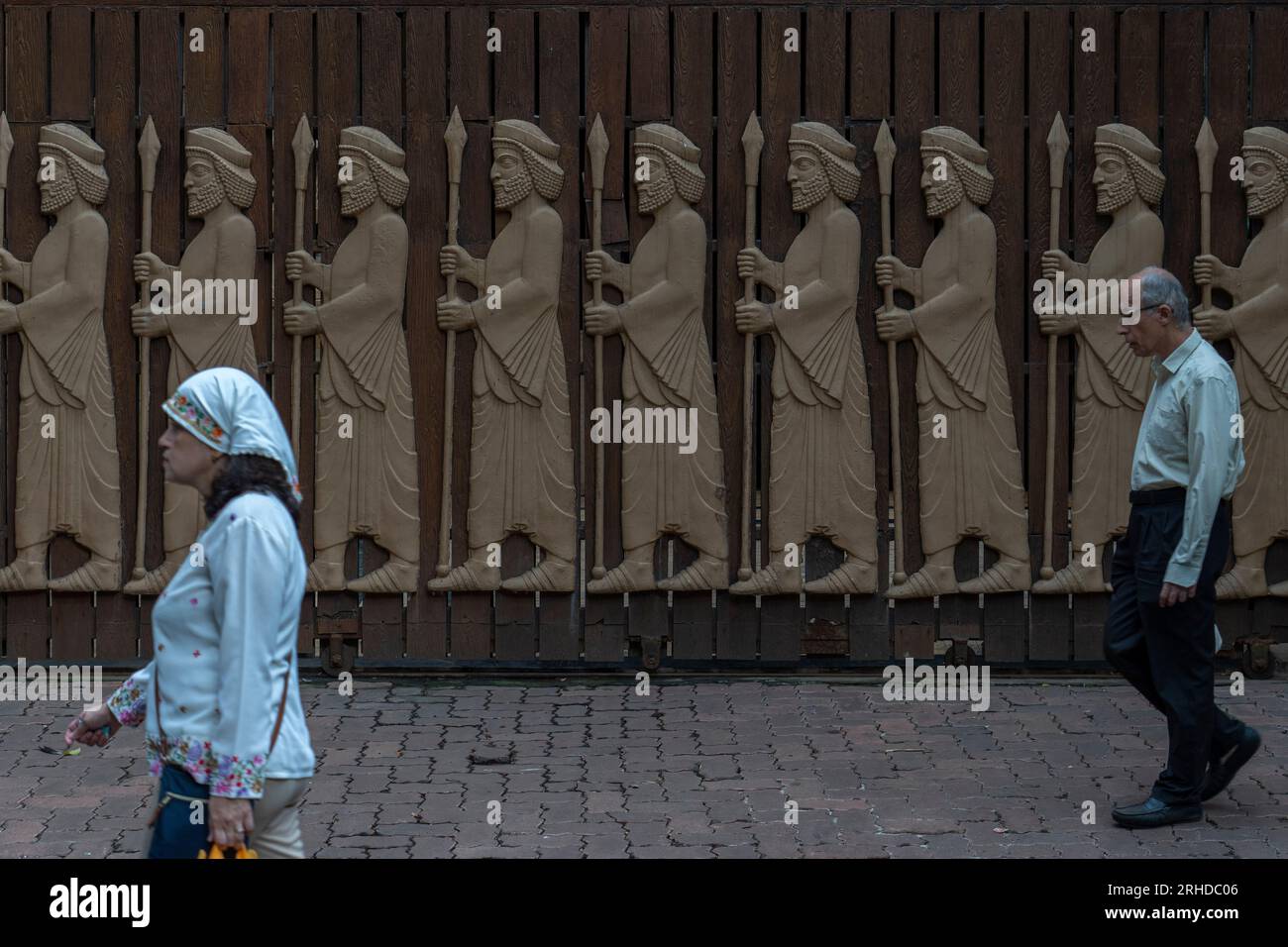 Parsi community members walk next to a bas-relief depicting early ...
