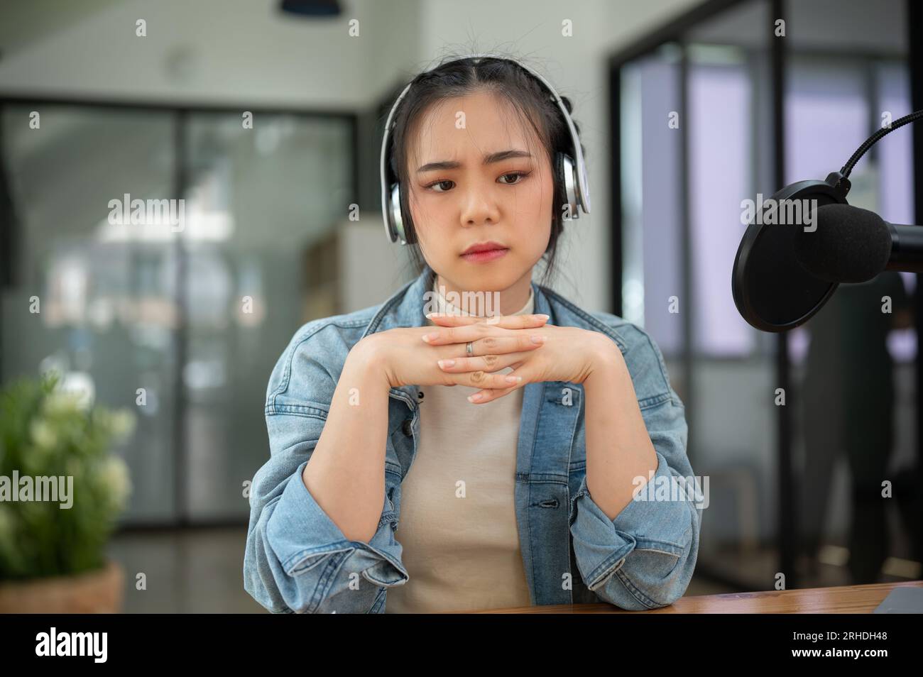 A stressed and serious Asian female radio host sits at her desk in the ...