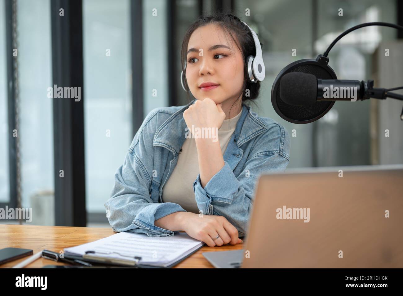 A beautiful and thoughtful Asian female radio host sits at her desk in ...