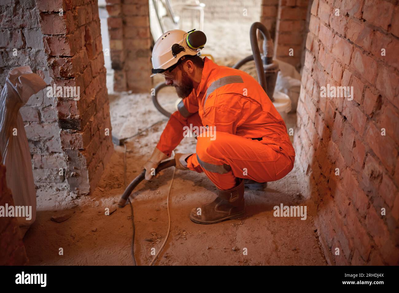 Constriction site worker cleaning concrete floor with special vacuum cleaner after demolishing ...
