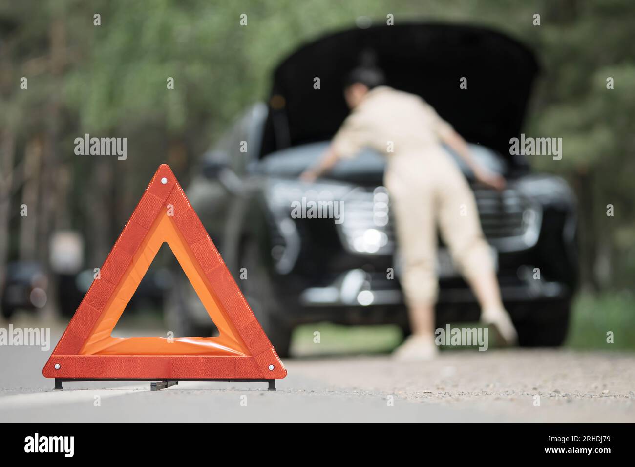 Warning triangle against woman driver trying to fix defect in engine ...