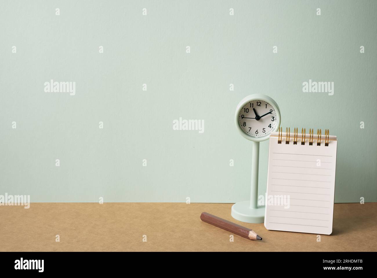 Notebook, colored pencil, clock on brown desk. mint green wall ...