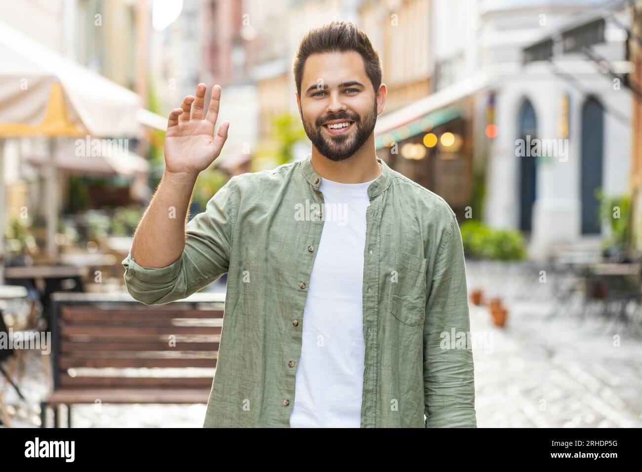 Bearded young man smiling friendly at camera, waving hands gesturing ...