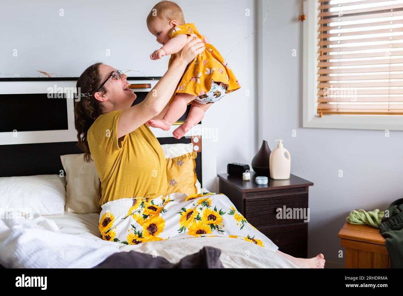 Mother in bedroom with baby girl playing together lifting child up into ...