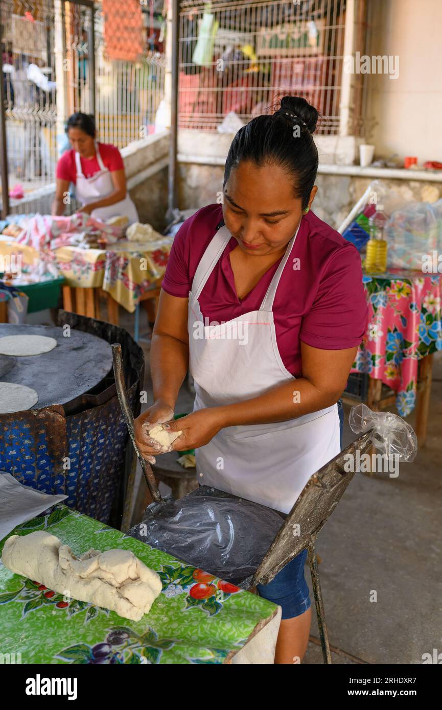 Mexican female cook kneading dough and rolling into ball near tortilla ...