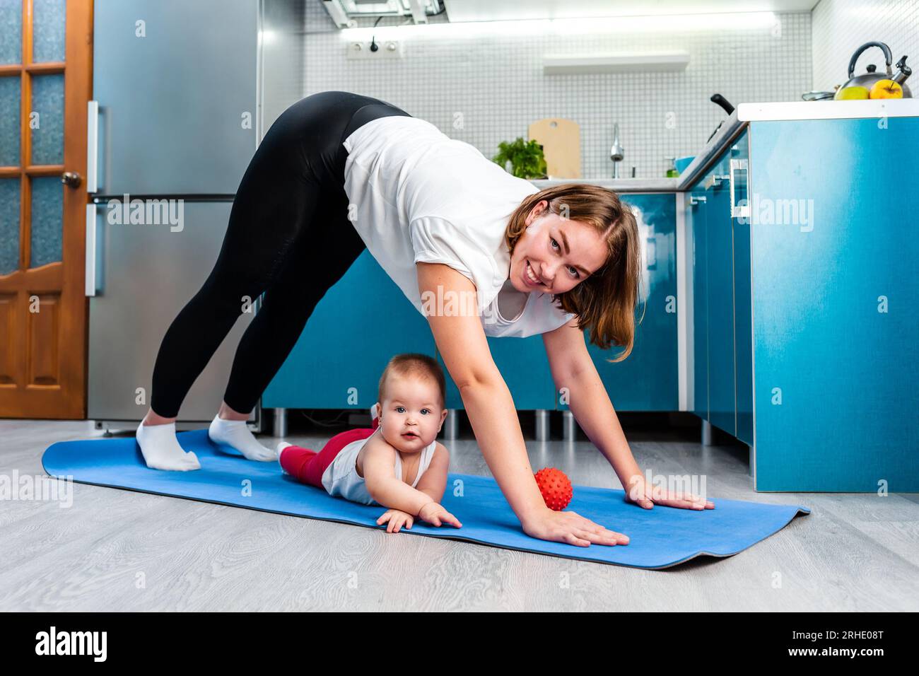 Home yoga. A young Caucasian mother does Adho Mukha Shvanasana while ...