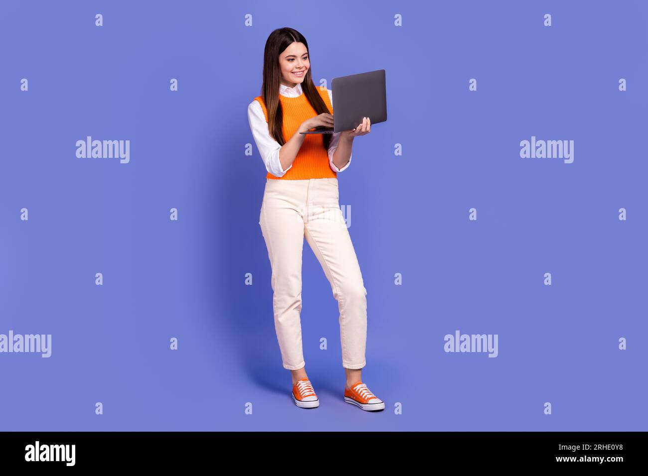 Full body cadre of schoolgirl wearing orange vest user laptop apple ...