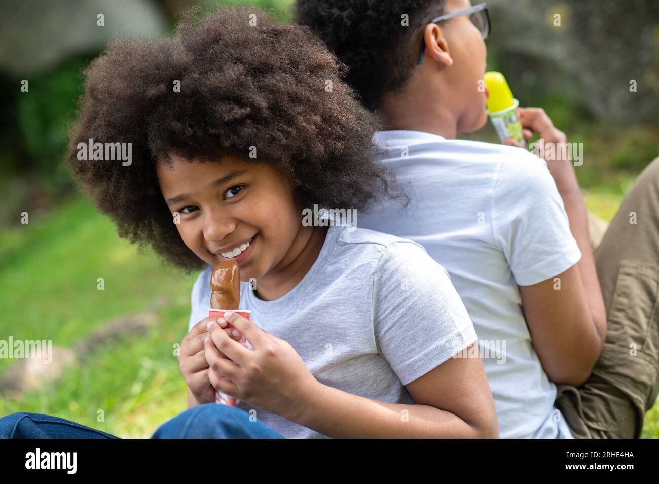 Two children eating ice cream in park sitting on green grass Stock ...