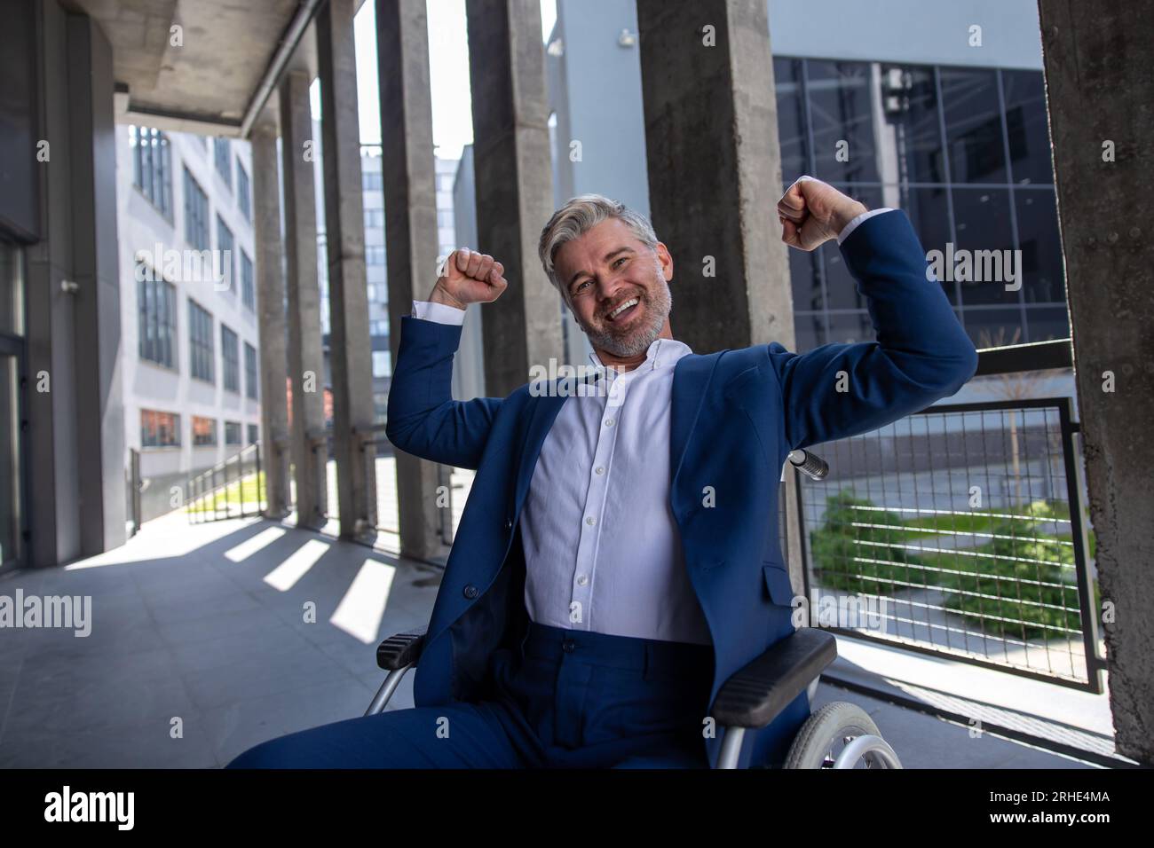 Strong gray haired disabled man wearing suit in wheelchair, rised arms ...